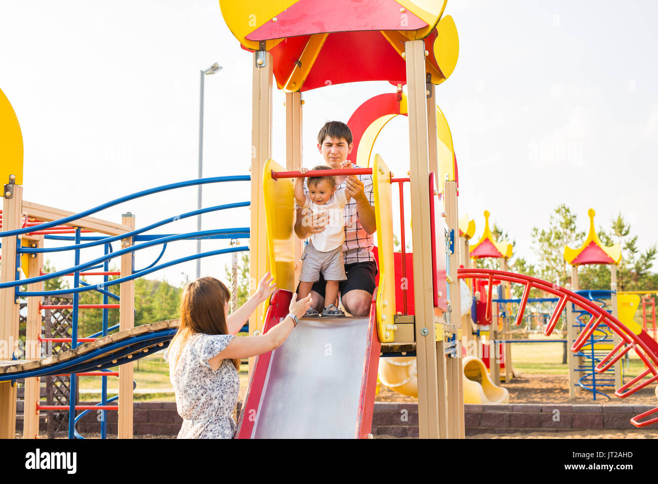 playful child with parents at the playground outdoor. Mom, dad and ...