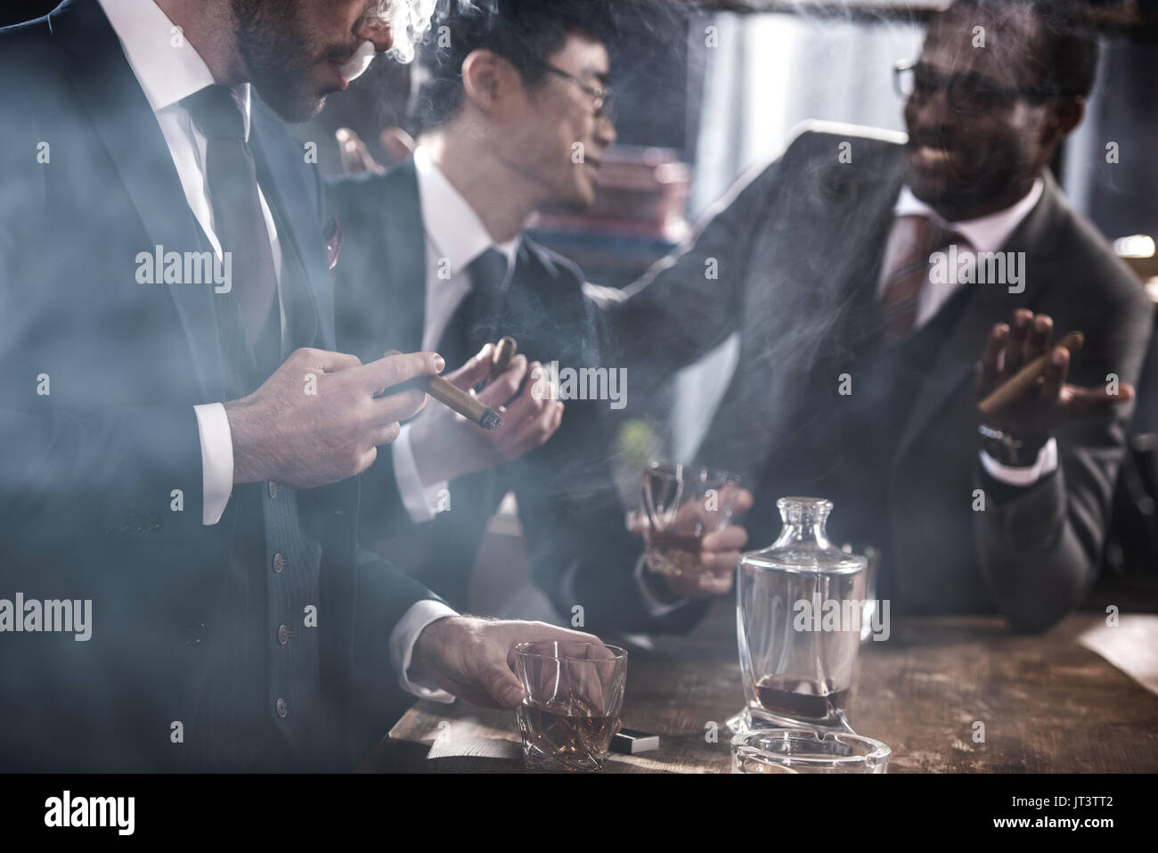multicultural business team spending time, smoking cigars and drinking ...