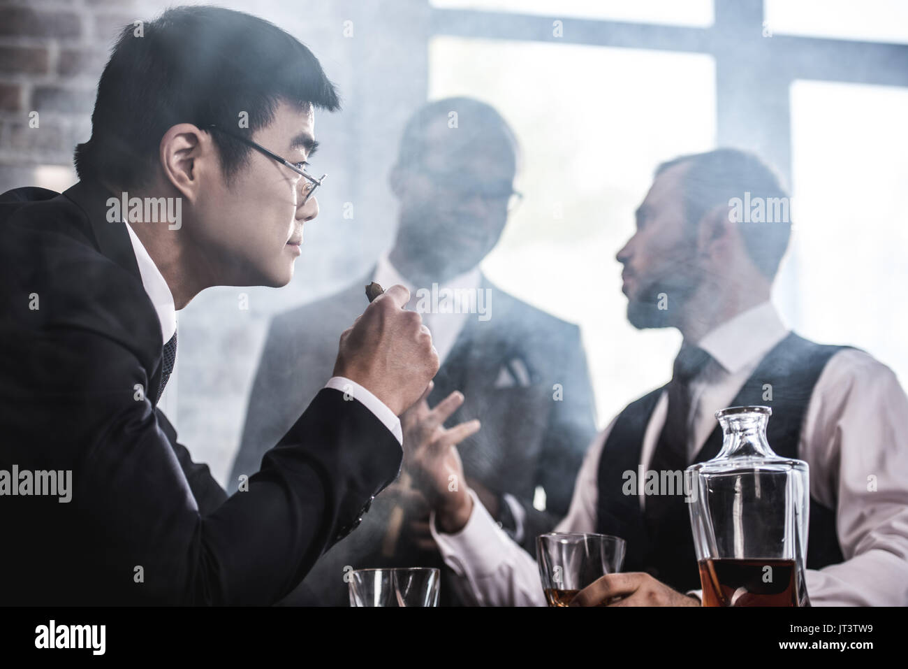 Multiethnic group of businessmen smoking and drinking whisky indoors ...