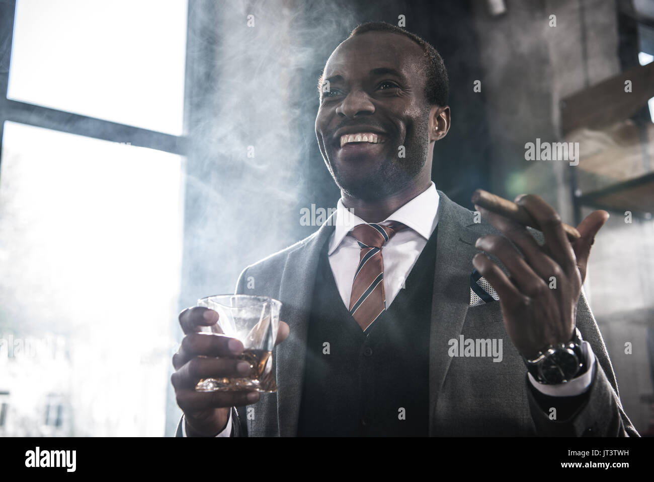Smiling african american businessman holding glass with whiskey and ... Smiling african american businessman holding glass with whiskey and ...