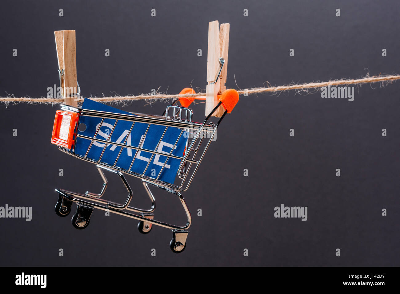 Close-up view of small shopping cart with sale sign hanging on rope ...