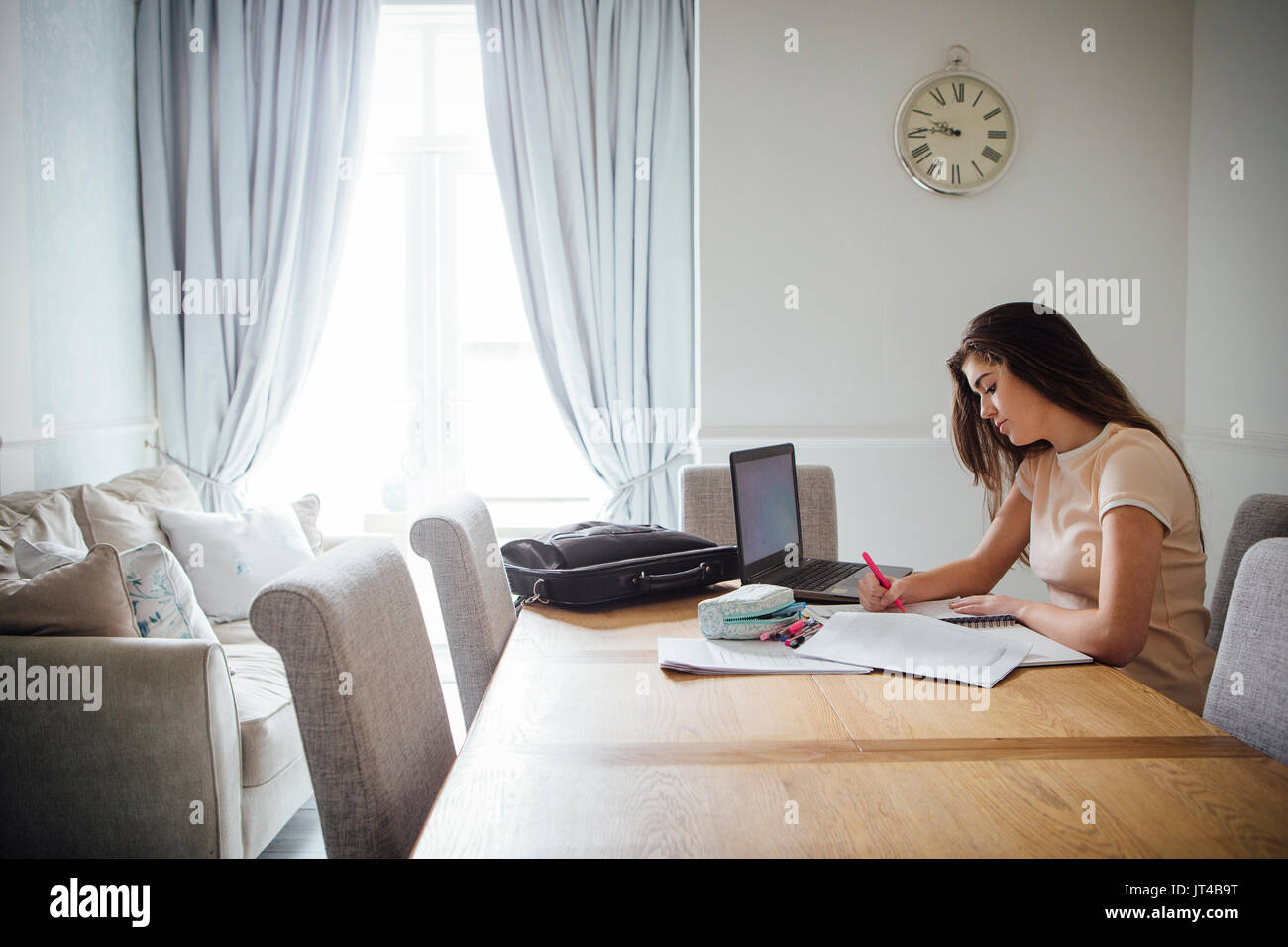 Teenage girl sitting at the table at home with her laptop, doing her ...