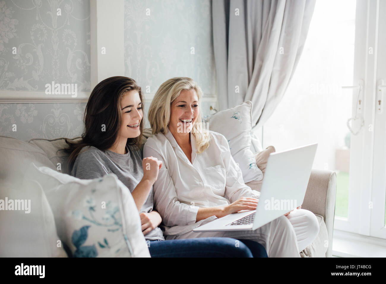 Mother and her daughter video calling someone on their laptop. They are ...