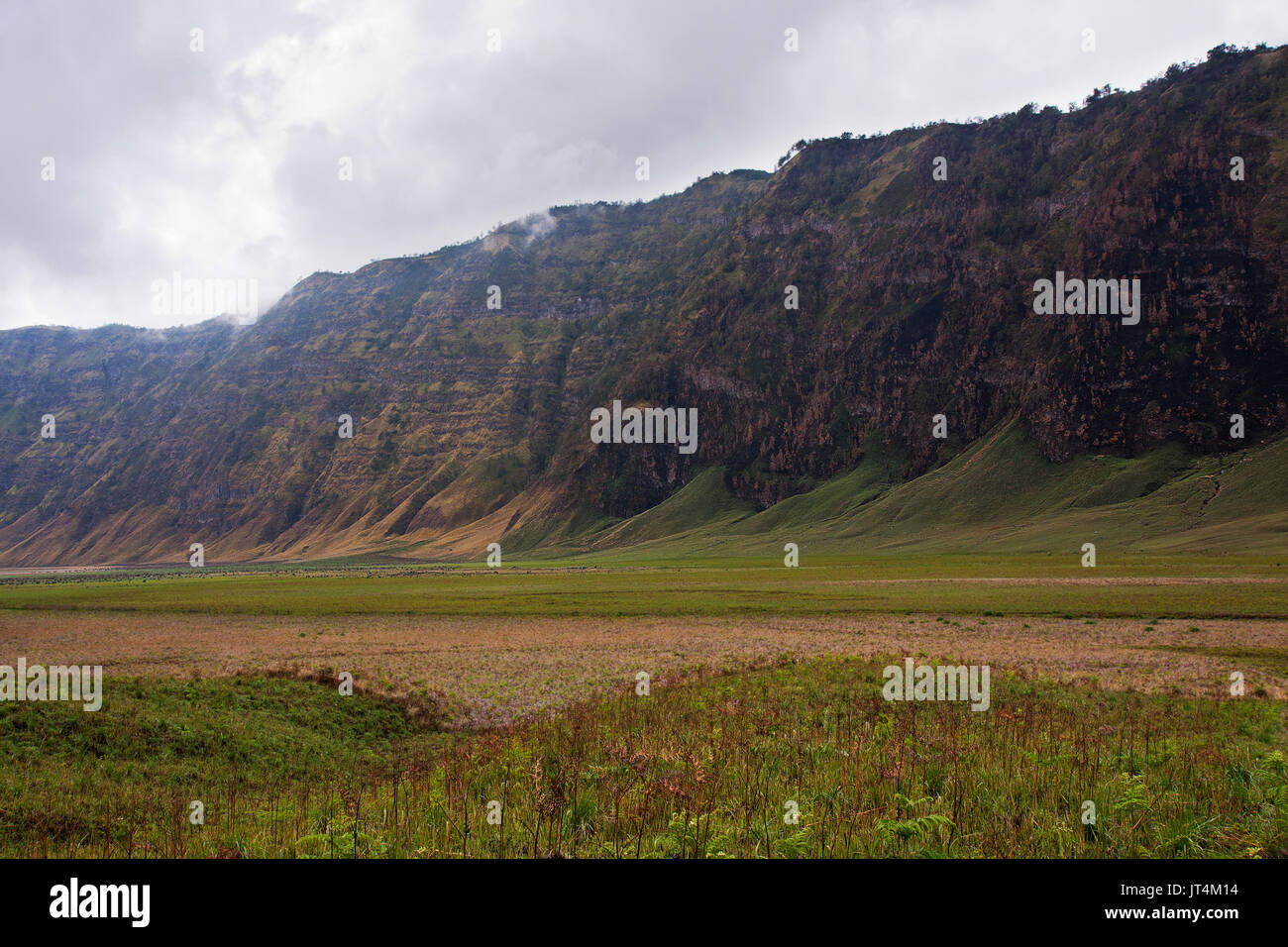High brown steep cliff next to green grass field savannah with hills ...