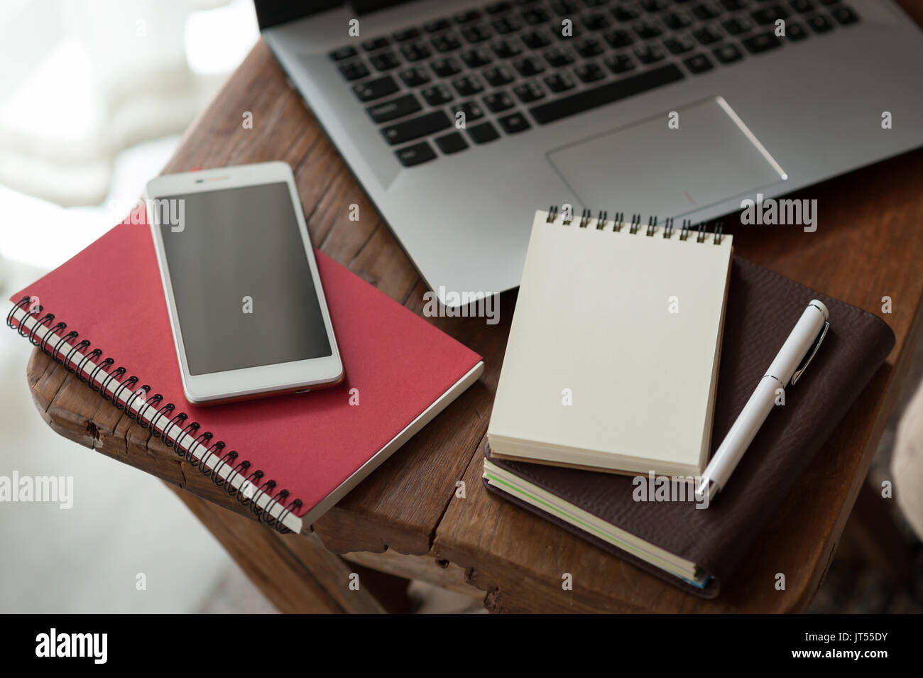 Pen, notebooks, smartphone, and laptop computer on small wood table ...
