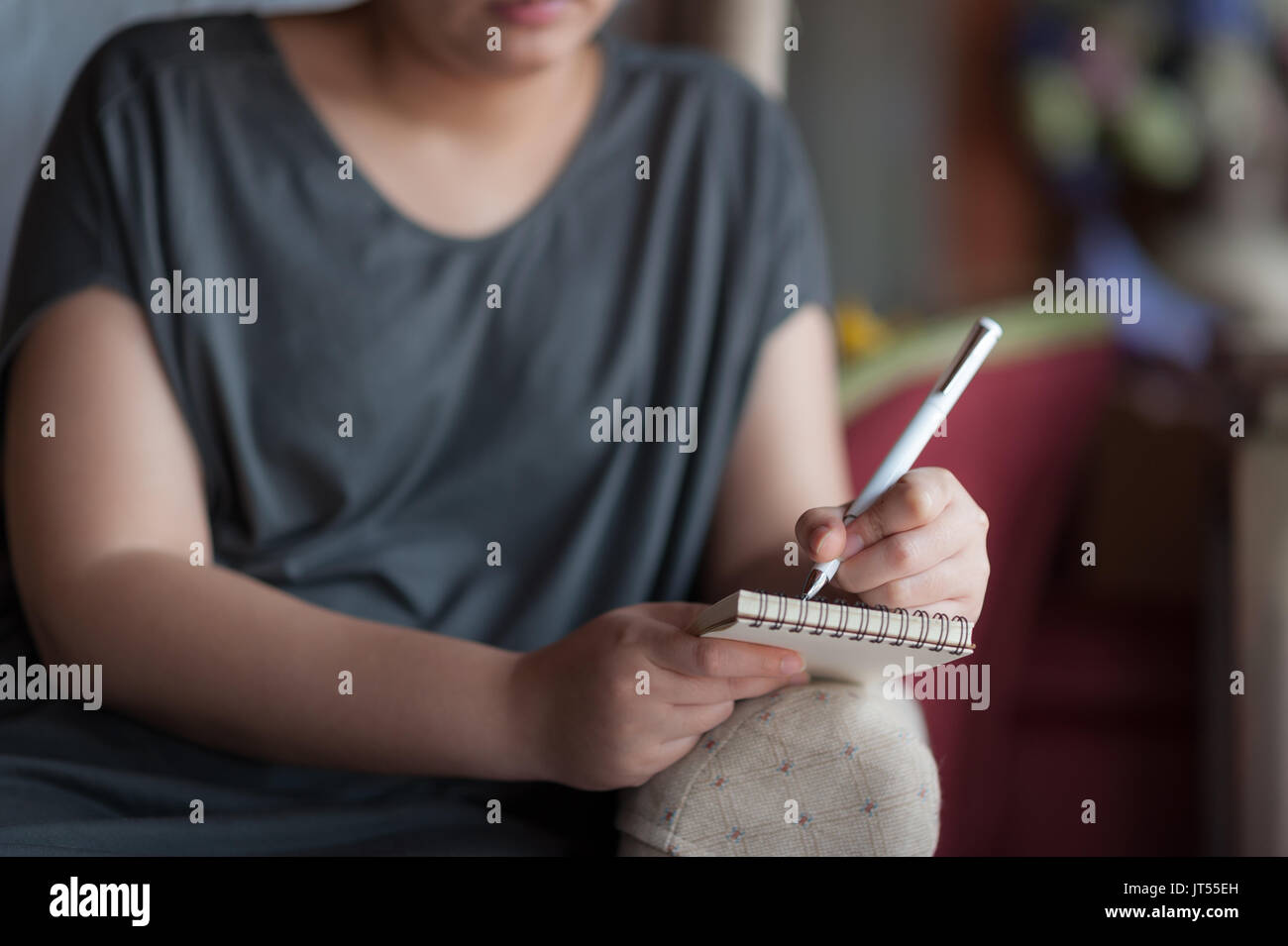 Left-handed woman writing some idea on small notepad while sitting on ...