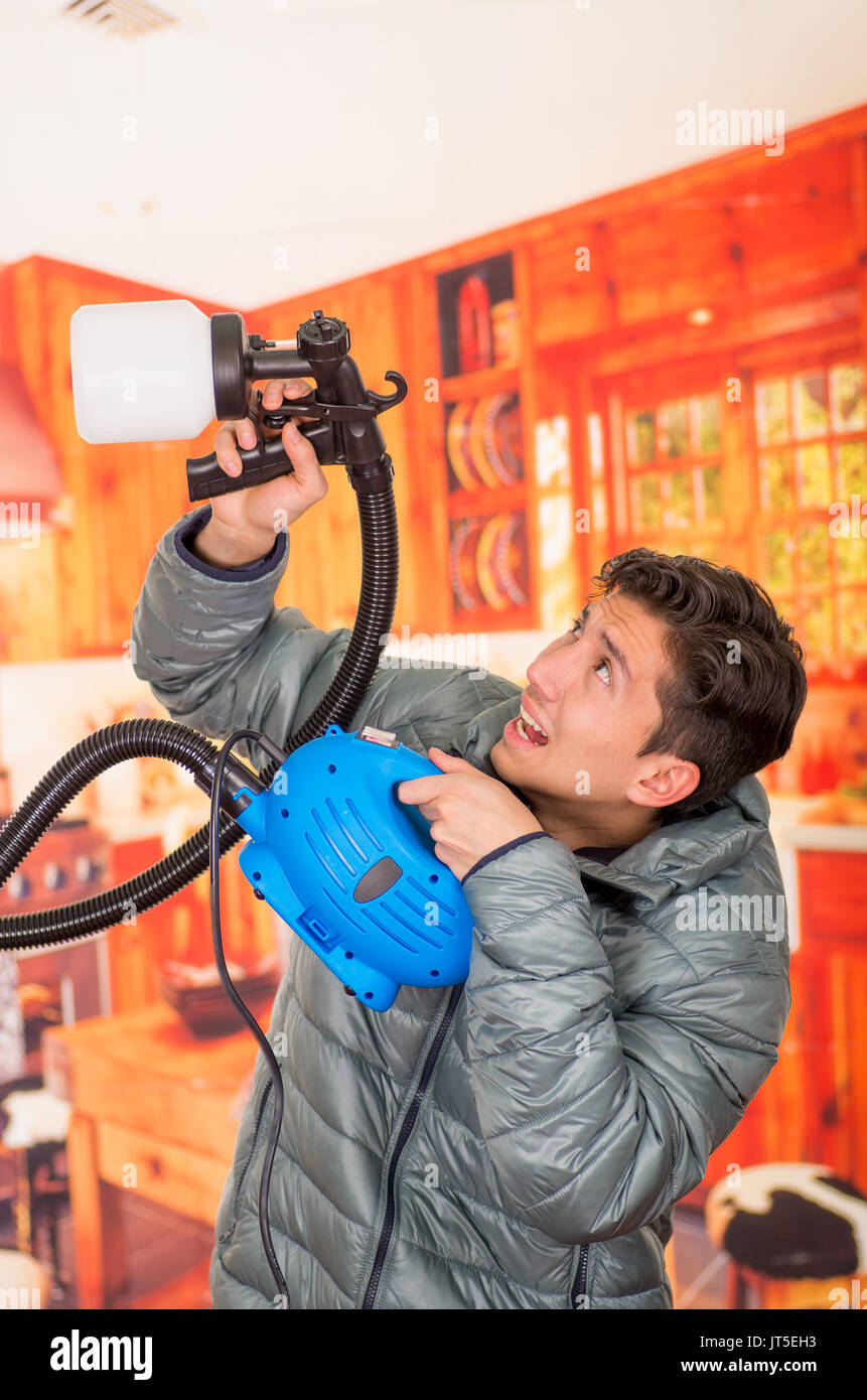 Handsome scary handyman holding in his hands the painting spray gun ...