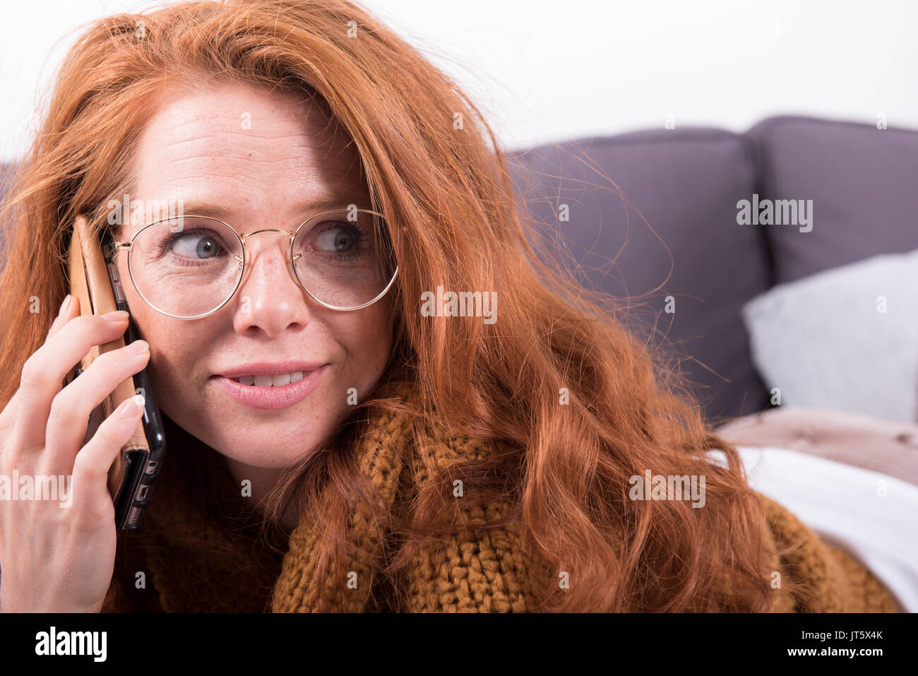 Beautiful, red-haired woman with orange sweater talking on the bed ...
