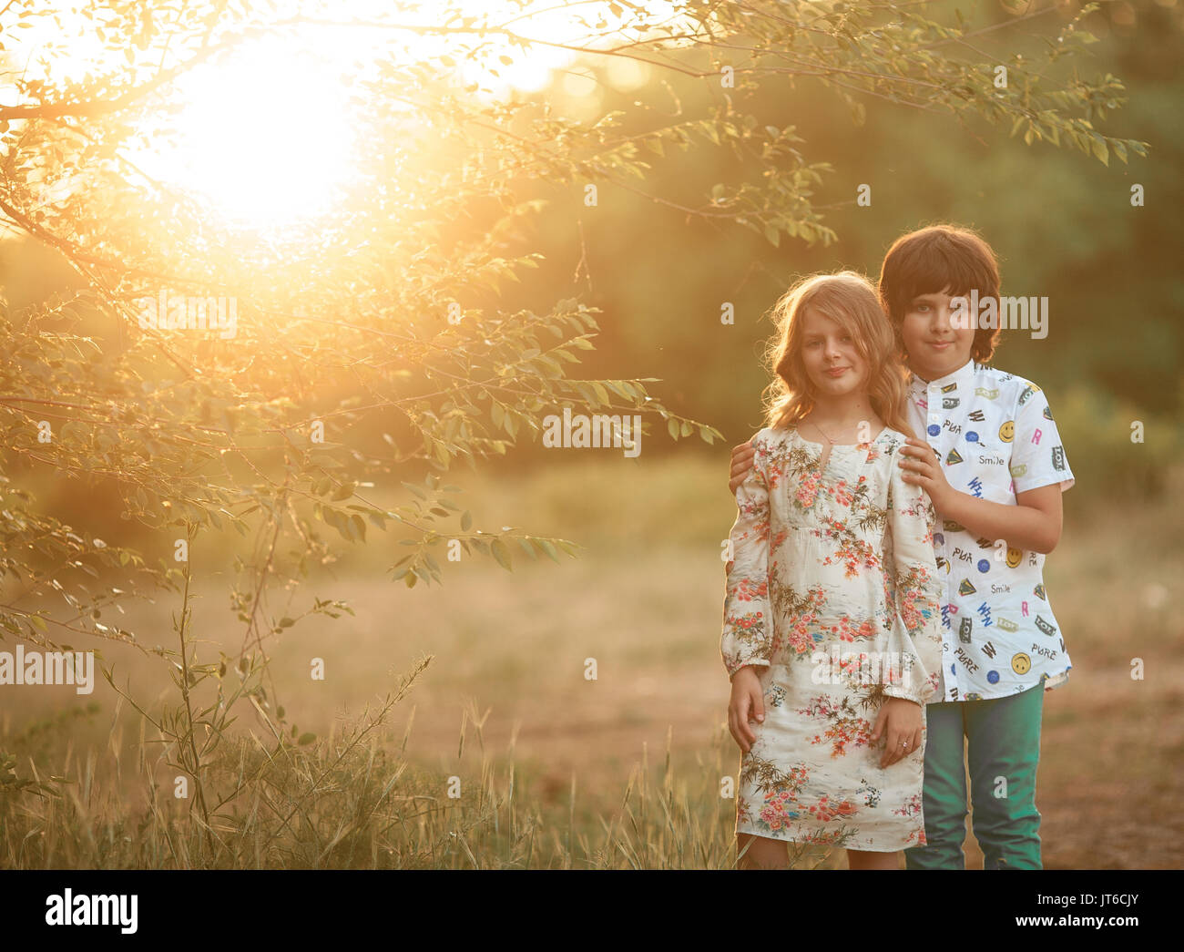 Little boy stands with girl in forest at sunset and holds her by ...