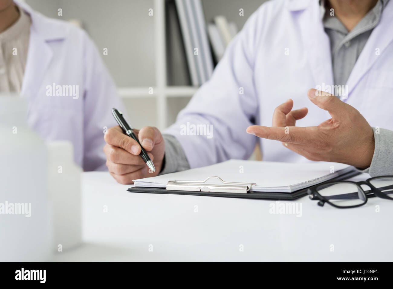 Two doctors discussing patient notes in an office pointing to a ...