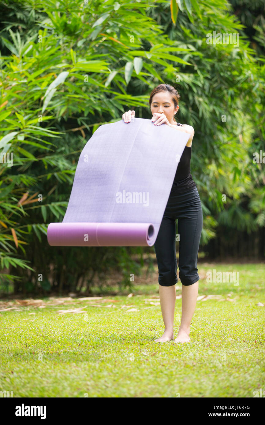 Asian woman laying out her yoga mat, getting ready to practice yoga ...