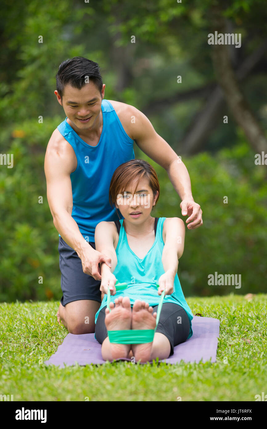 Asian woman with a personal trainer doing exercises outdoors. Action ...