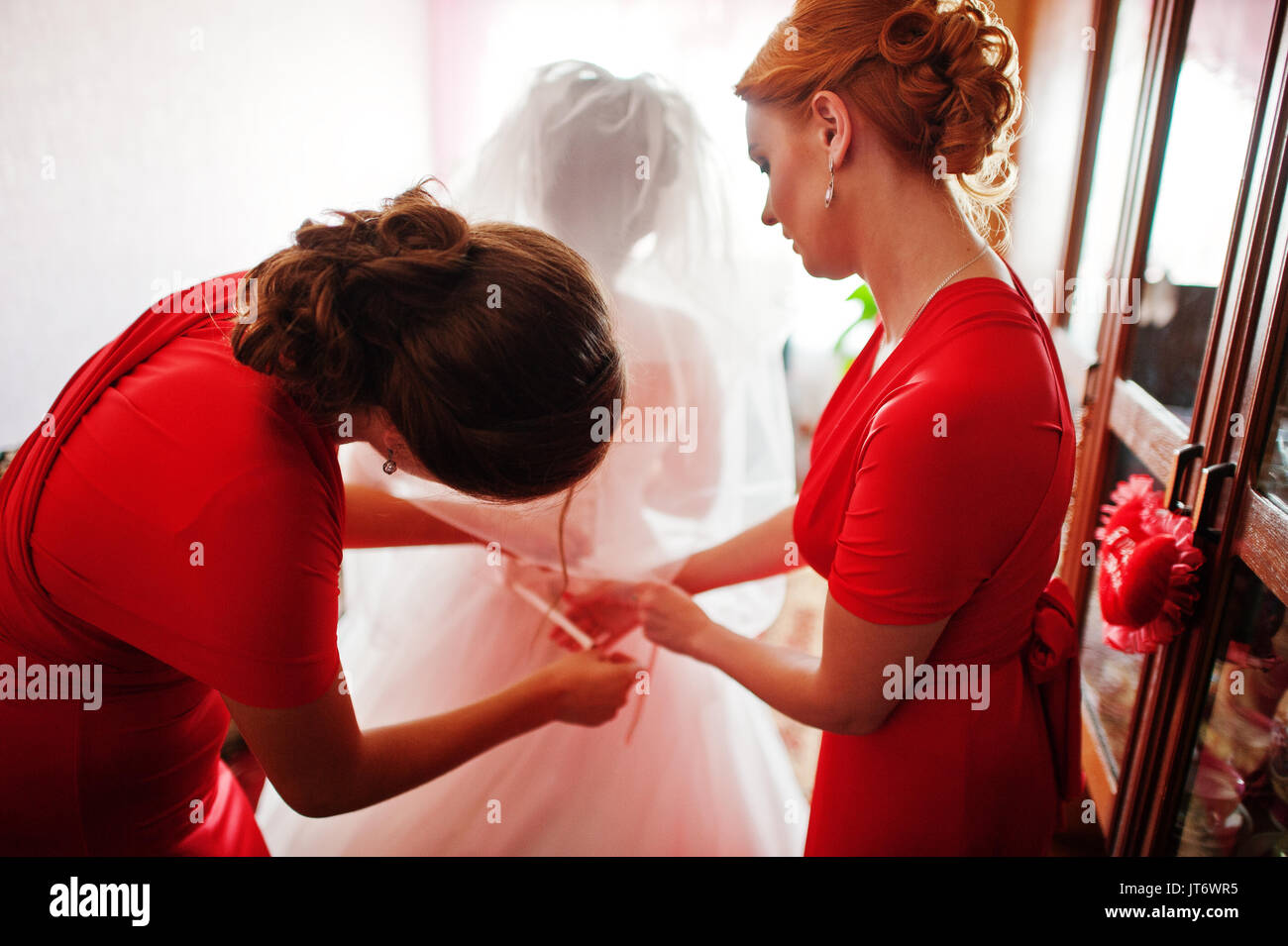 Helpful bridesmaids helping bride to dress up and get ready for her ...