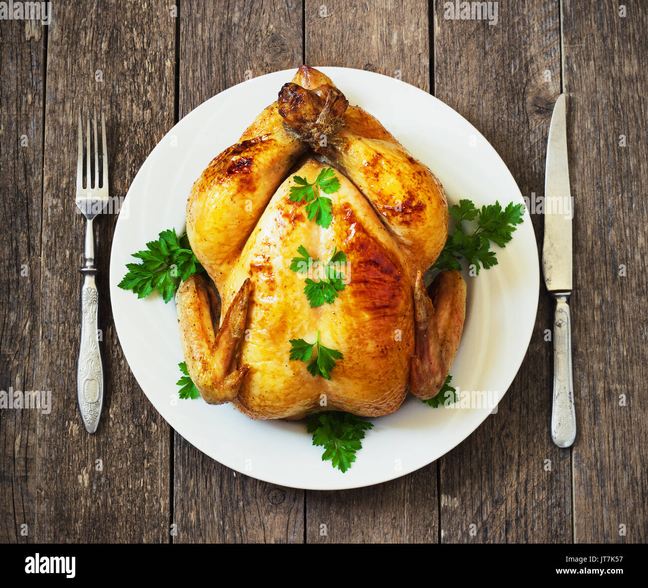 whole roasted chicken with tomatoes and cutlery on a wooden table Stock ...