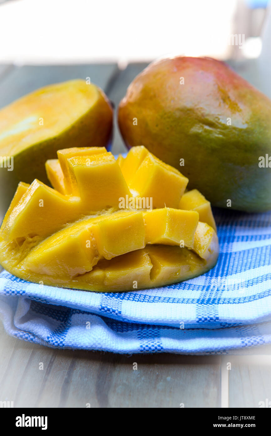 Fresh ripe raw mangos one is cut into cubes on a rustic wood table top ...