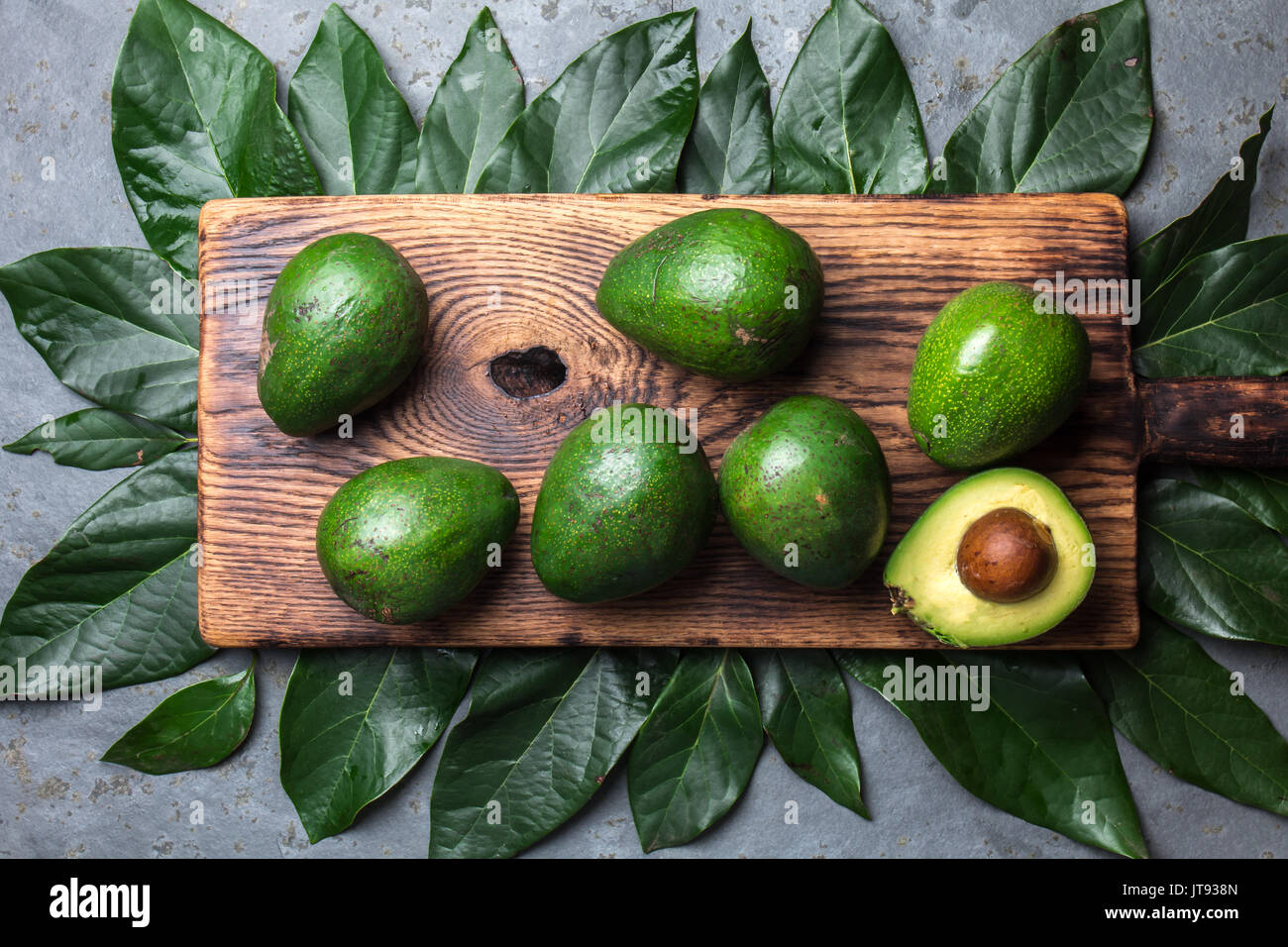 food background with fresh avocado, avocado tree leaves and wooden ...