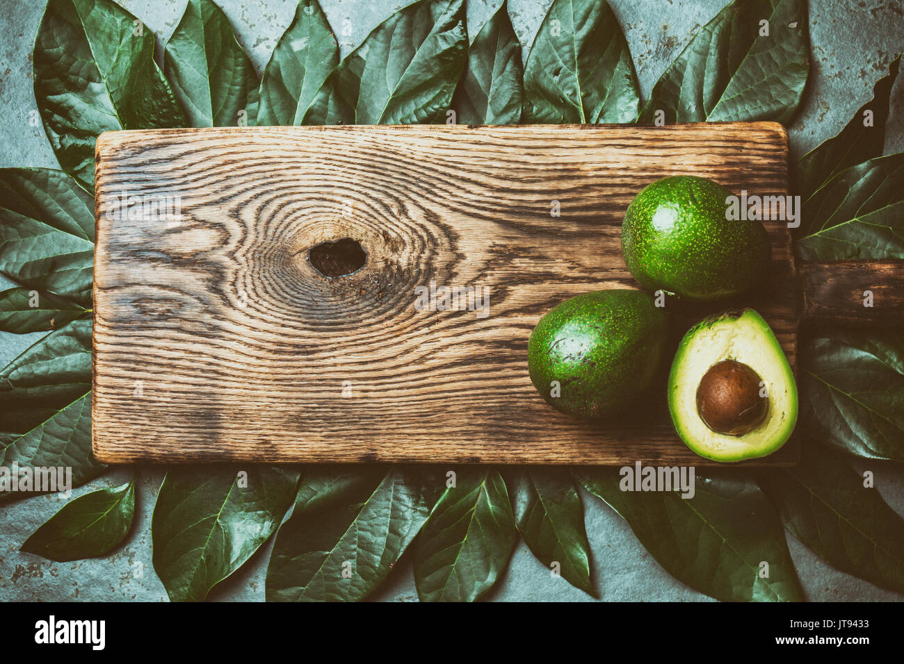 food background with fresh avocado, avocado tree leaves and wooden ...