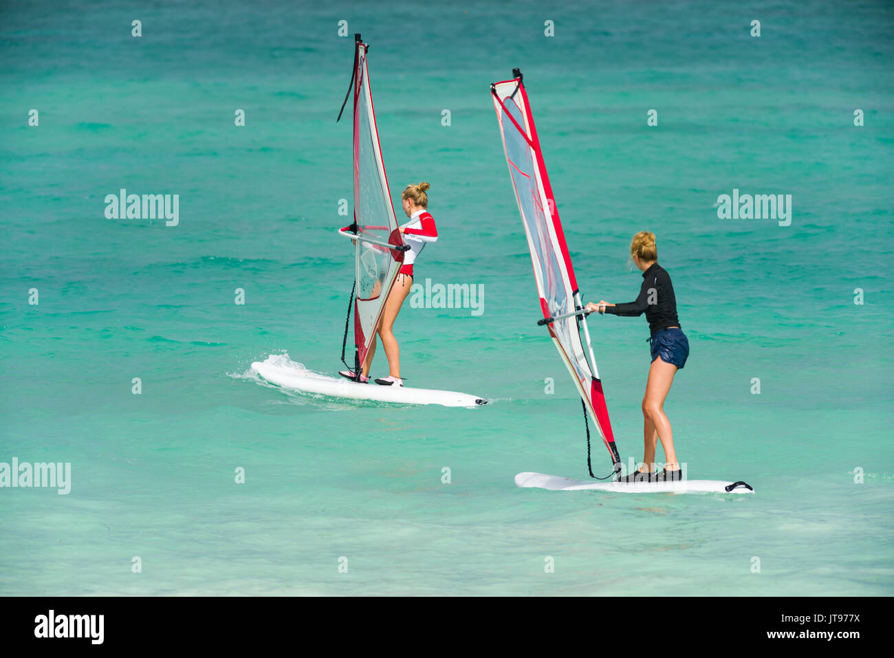 Two young Caucasian female windsurfers in the clear aqua waters of the ...