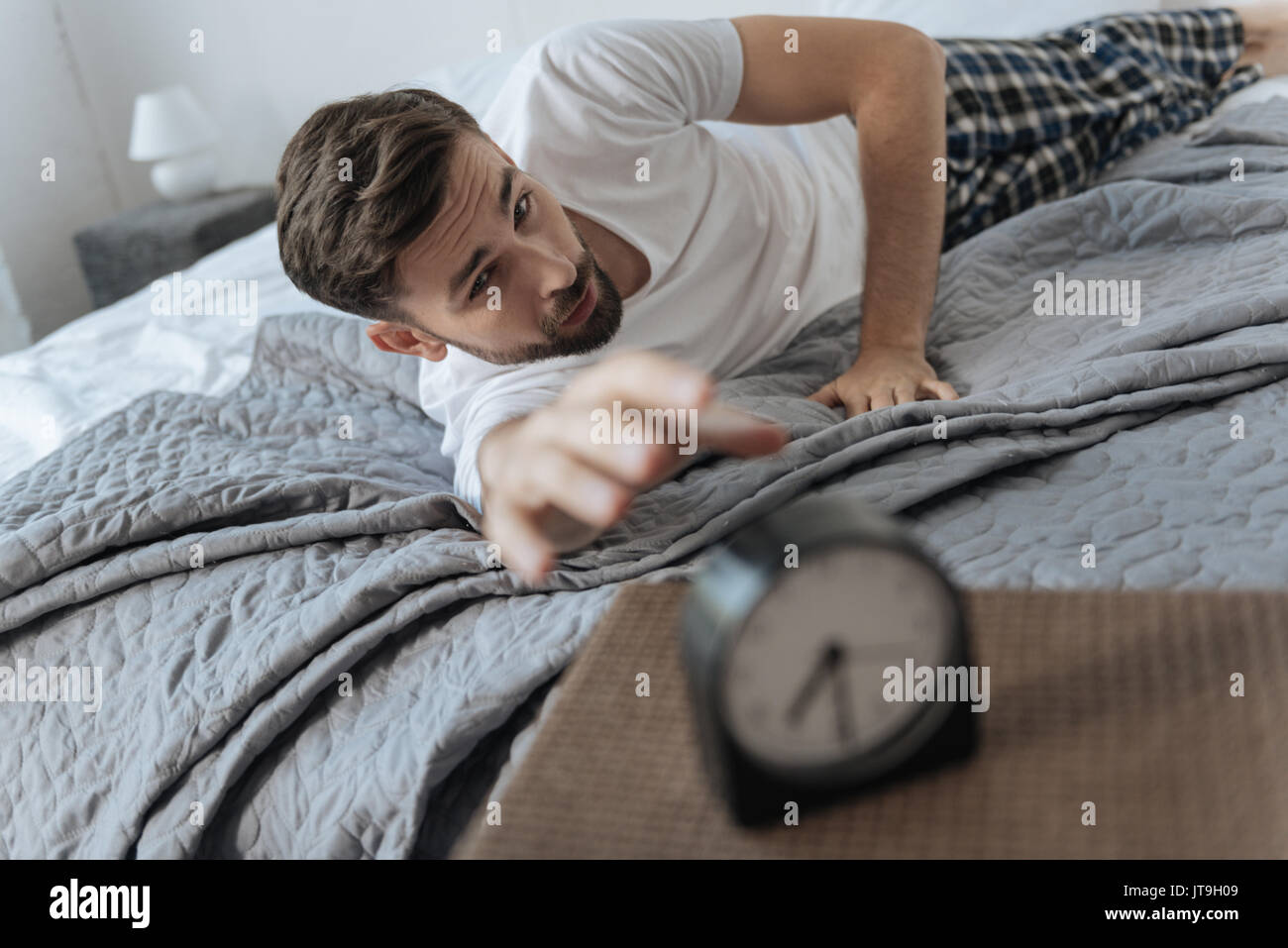 Sad unhappy man trying to reach the alarm clock Stock Photo - Alamy