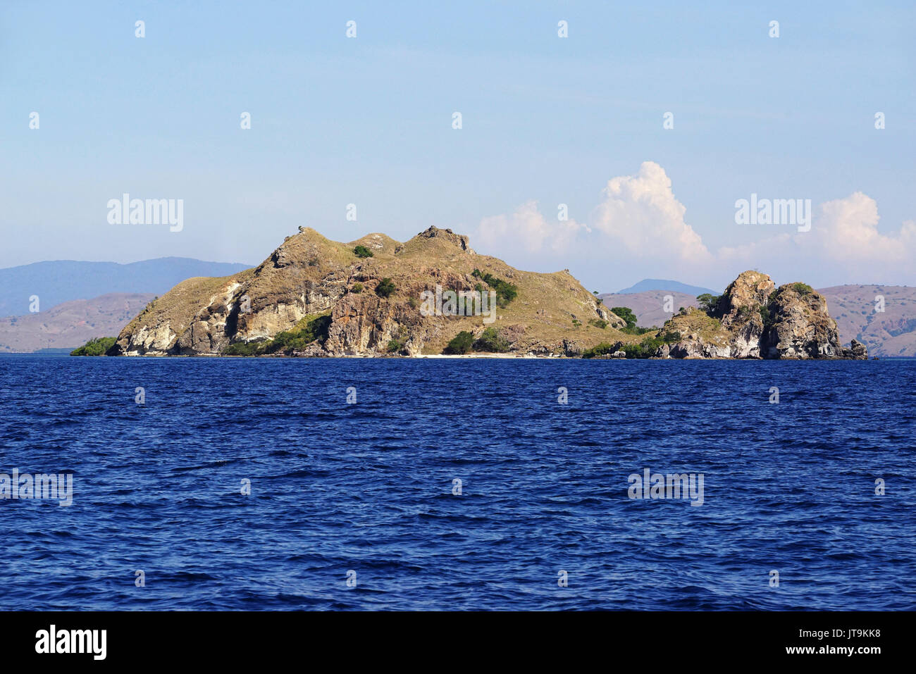 Small empty rock Island with green vegetation in the blue ocean water ...