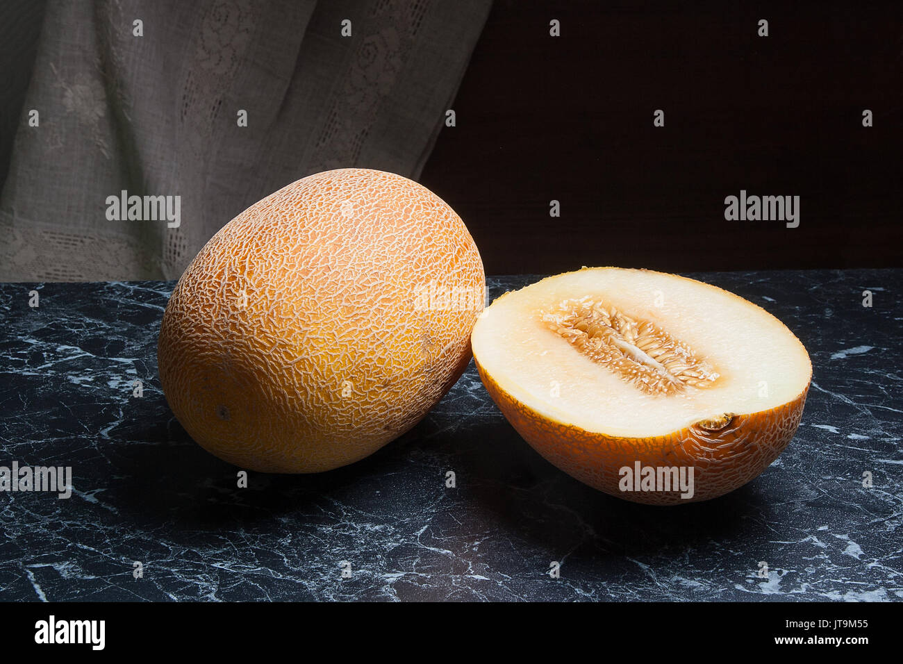 Ripe whole and half honeydew melon fruit at summer time on dark marble ...