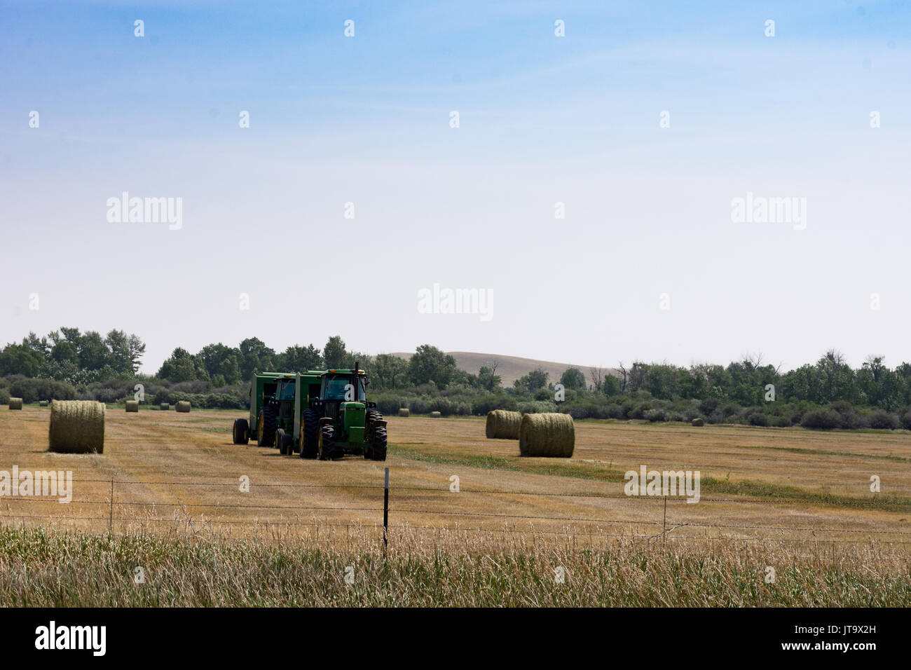 Tractor with baler and large round hay bales in a field in rural ...