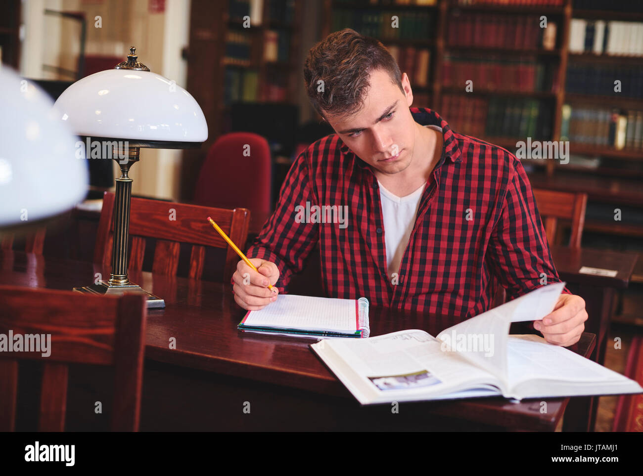 Man writing at desk in library Stock Photo - Alamy