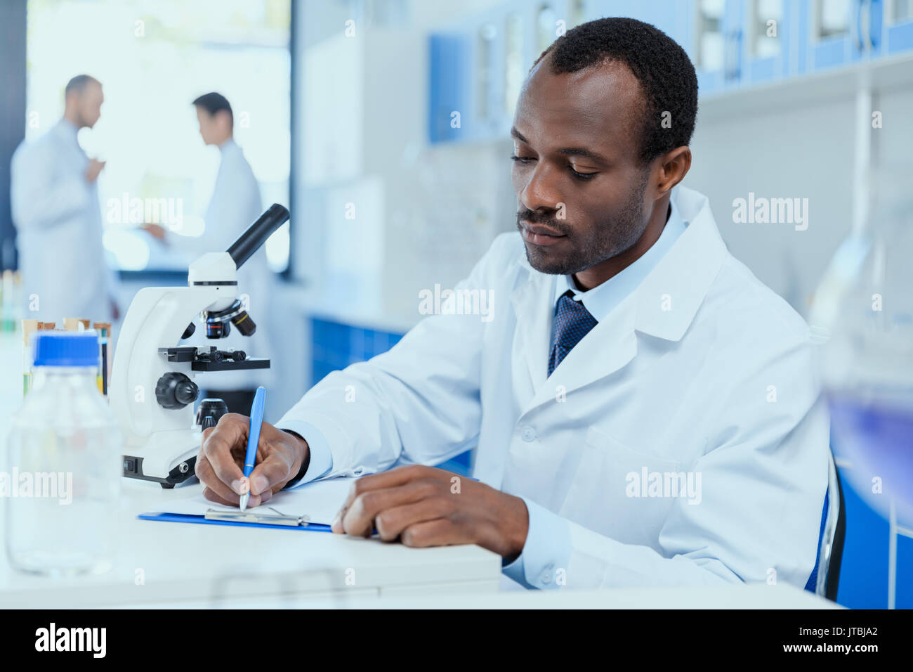 African american scientist in white coat taking notes while working in ...