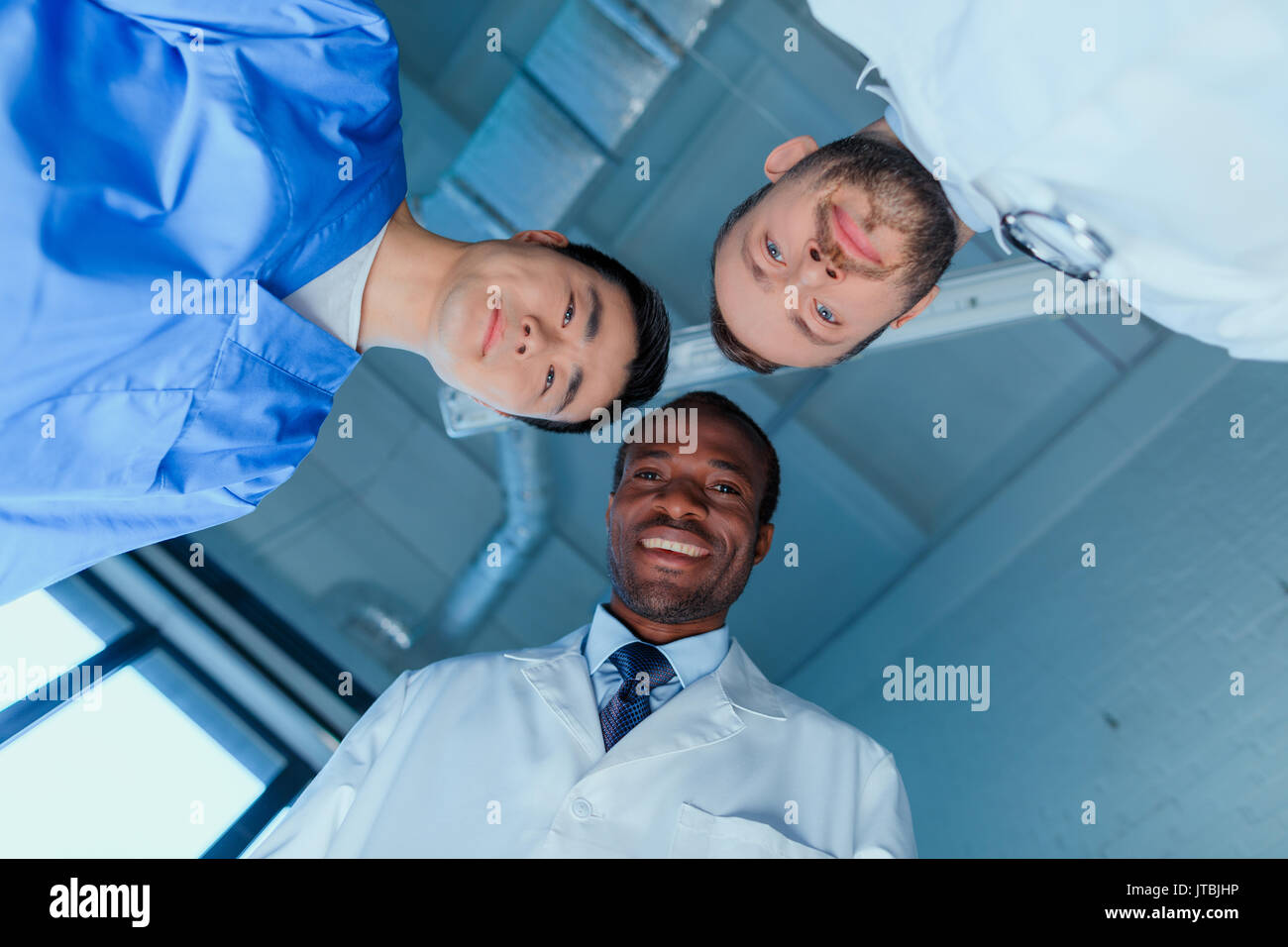 bottom view of multiracial group of doctors standing in circle in ...