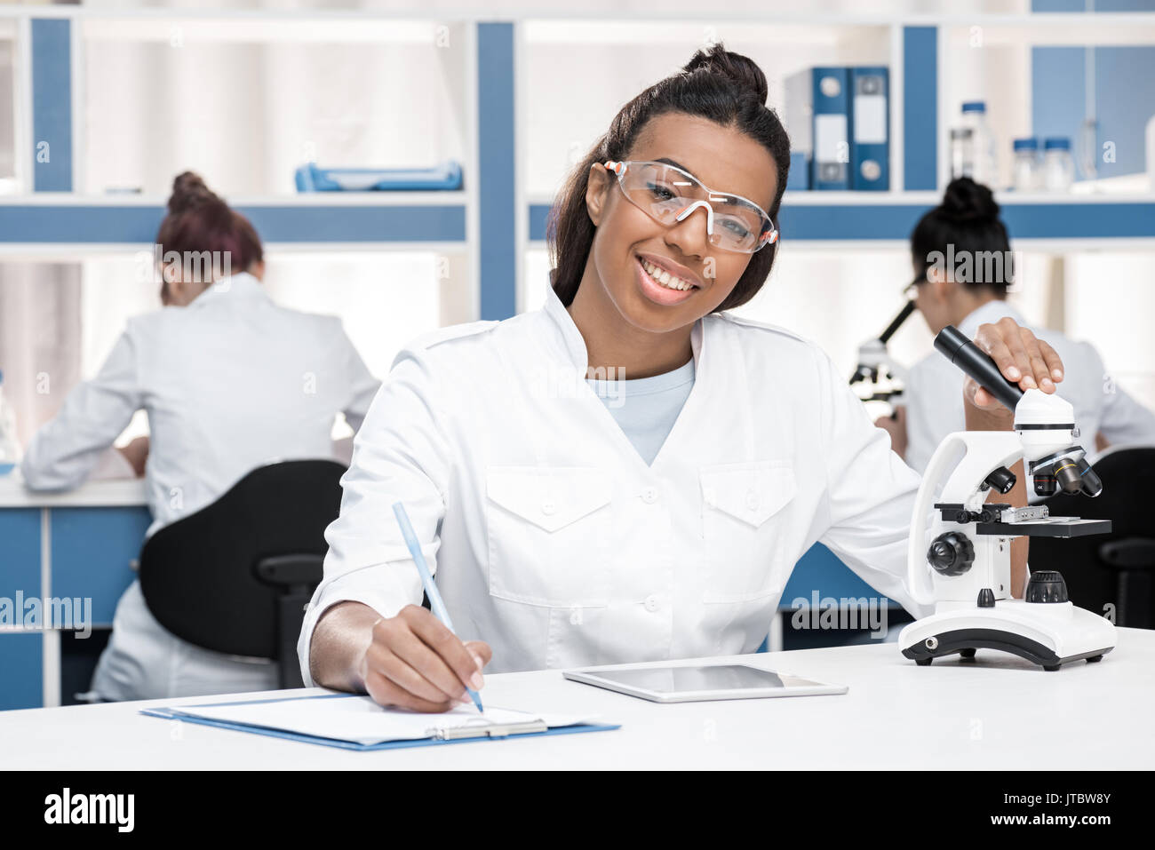 african american scientist in lab coat with clipboard, microscope and ...