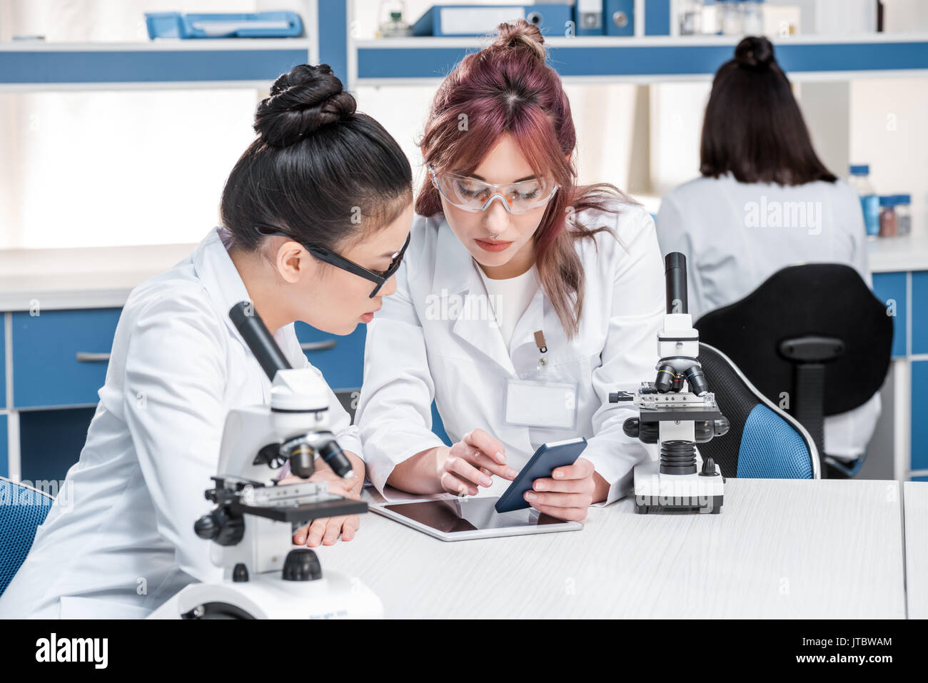 scientists working together with microscopes and smartphone in chemical lab, scientists team ...