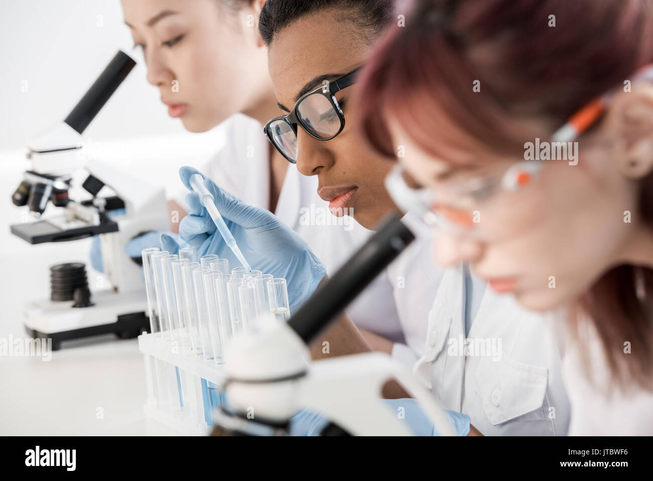 Multiethnic group of young professional scientists working with microscopes in chemical lab ...