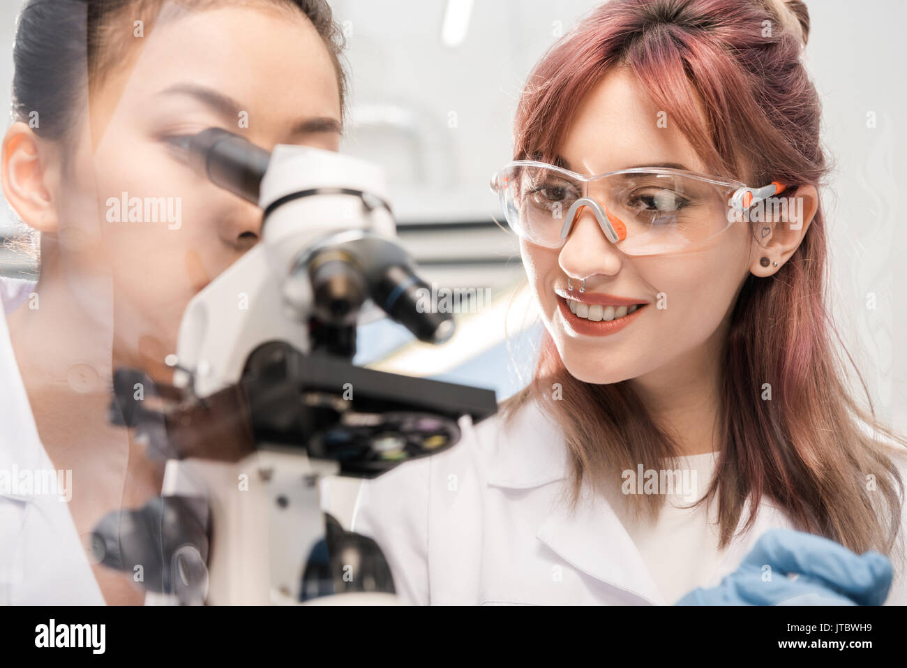 side view of woman scientist looking through microscope with colleague ...