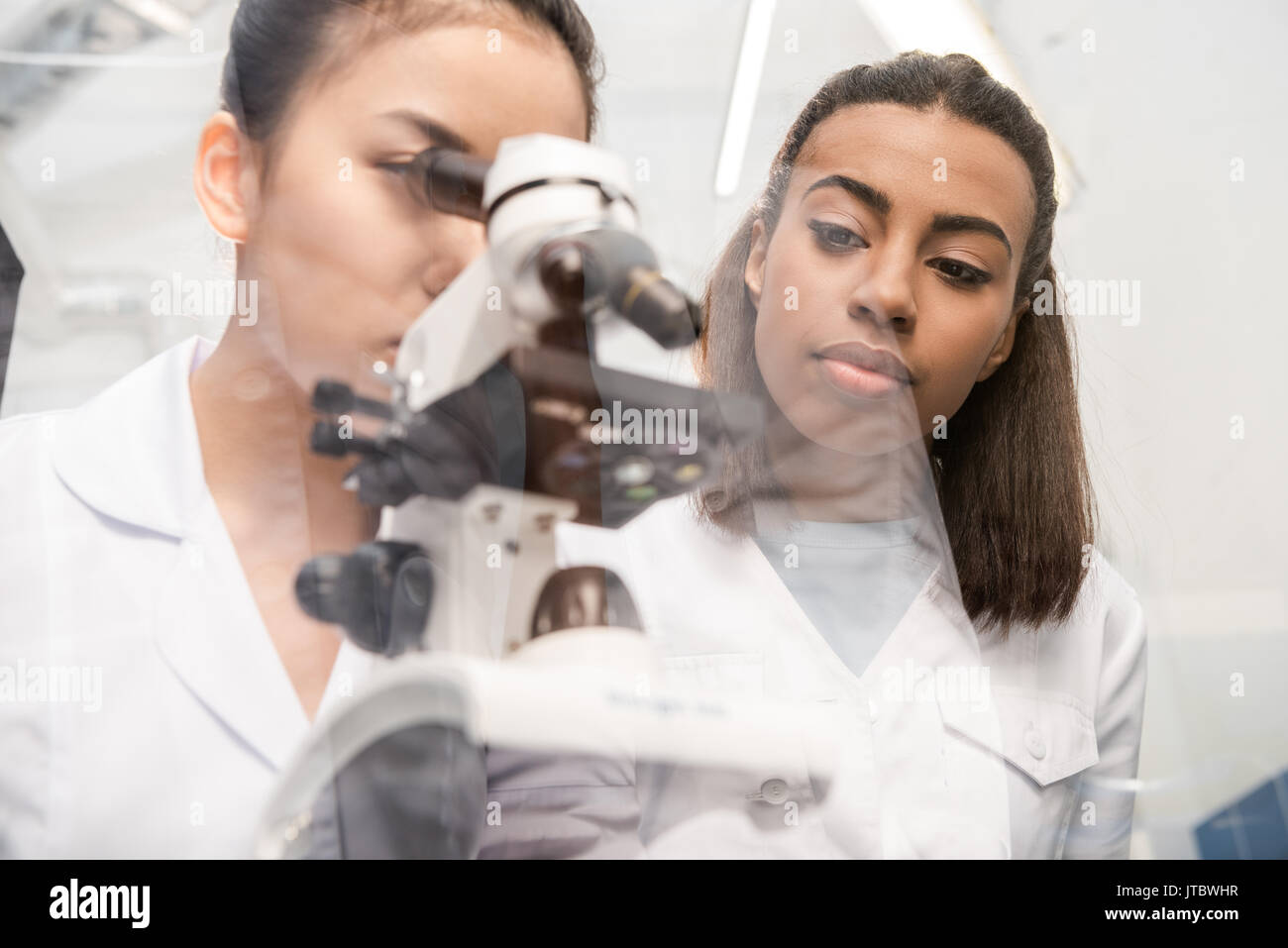 side view of woman scientist looking through microscope with colleague ...