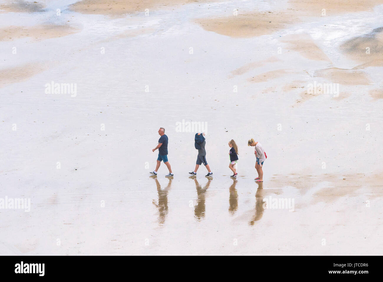 A family of holidaymakers walking in single file on a beach in Newquay ...