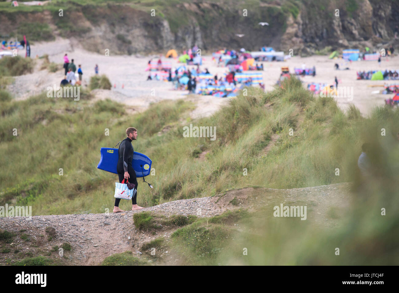 A holidaymaker carrying a bag and a body board and walking to the beach ...