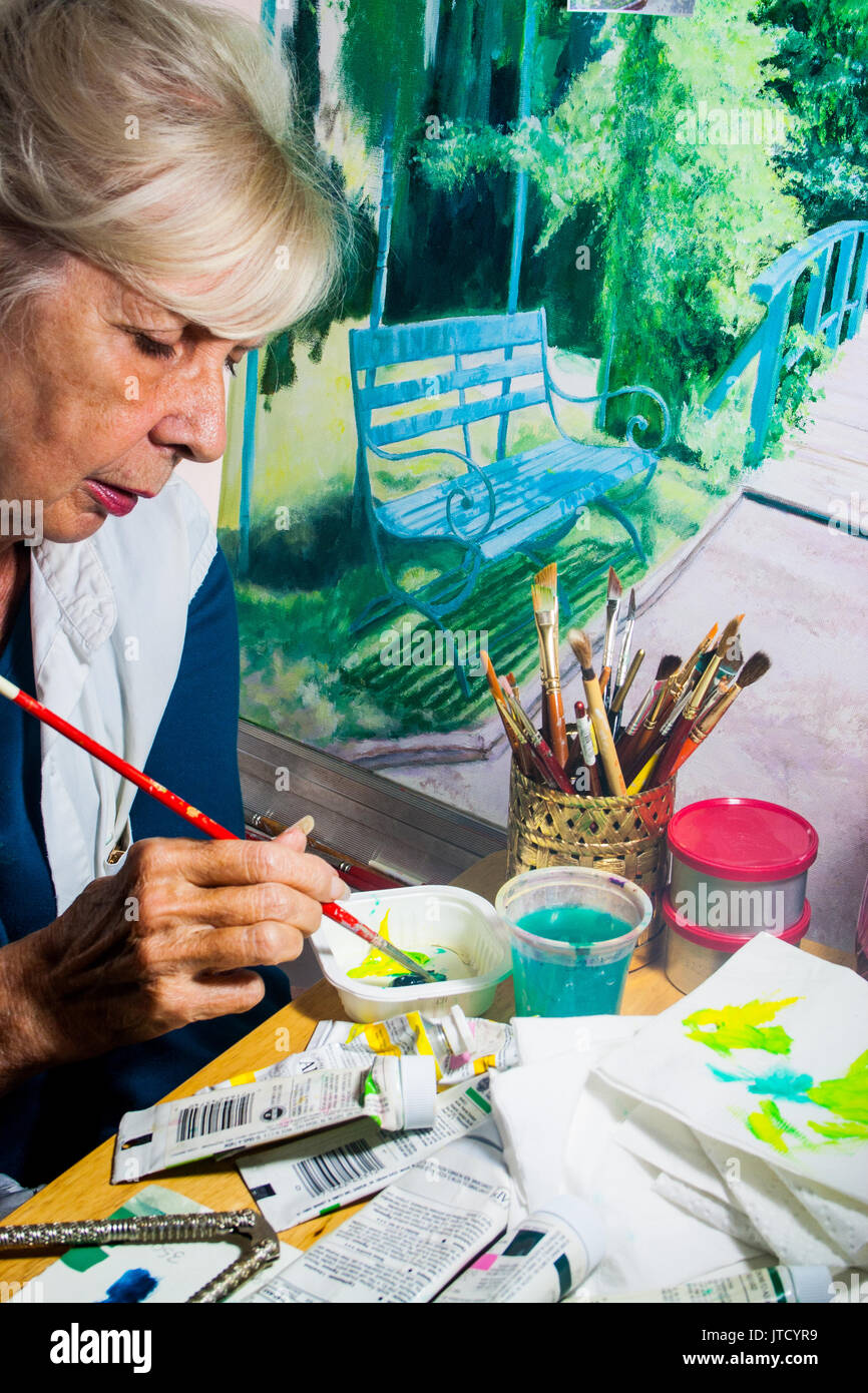 Blond, pony-tailed senior professional artist works on a canvas based ...