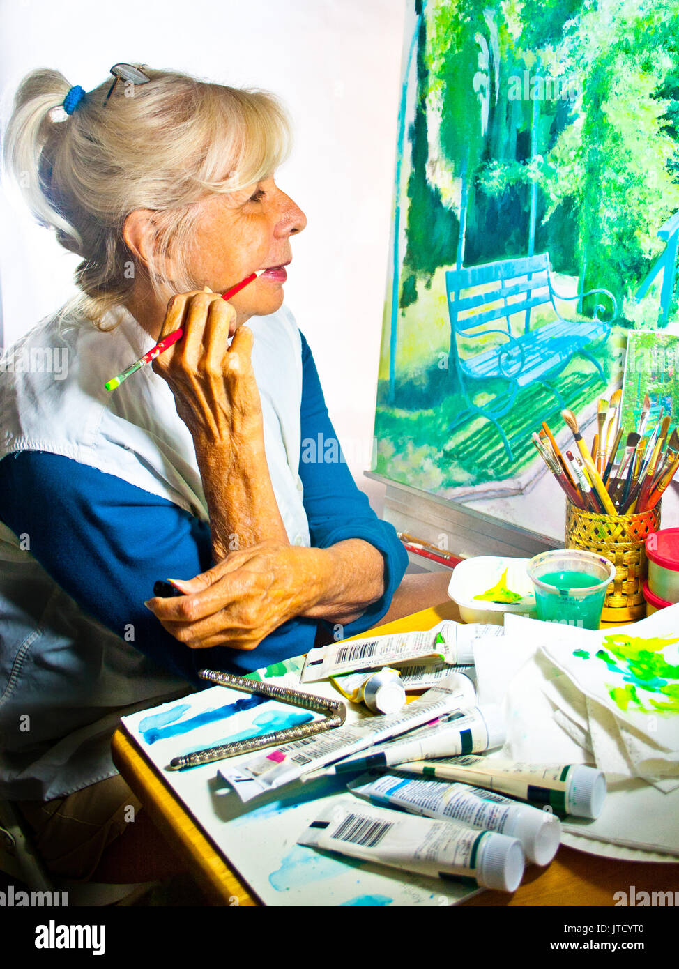 Blond, pony-tailed senior professional artist works on a canvas based ...