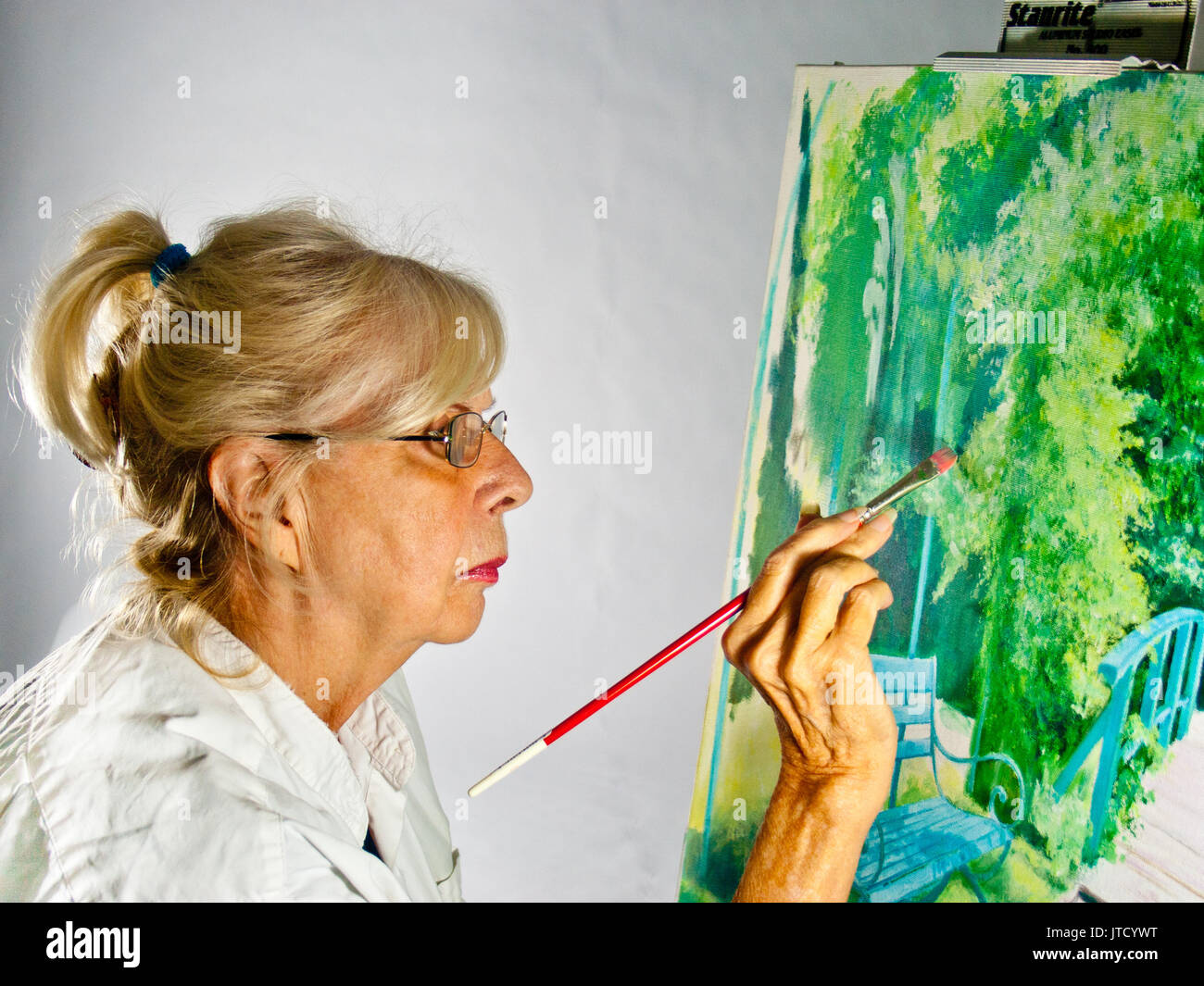 Blond, pony-tailed senior professional artist works on a canvas based ...