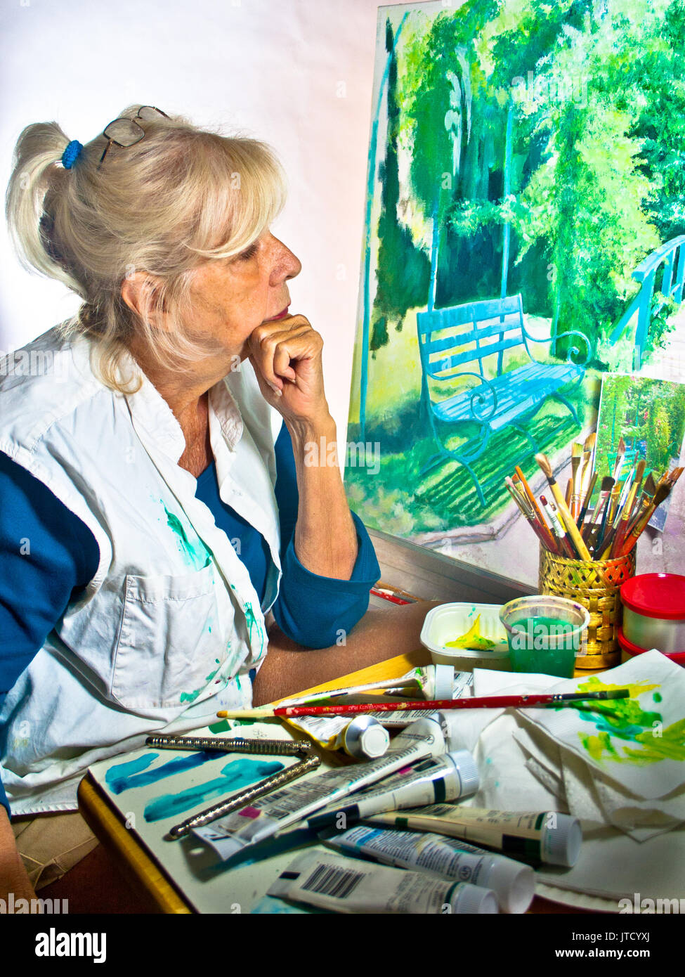 Blond, pony-tailed senior professional artist works on a canvas based ...