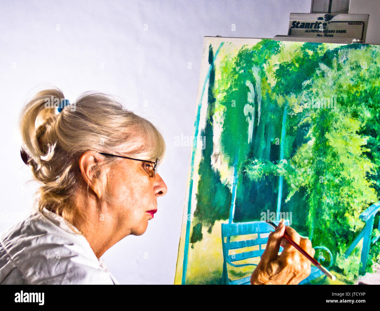 Blond, pony-tailed senior professional artist works on a canvas based ...