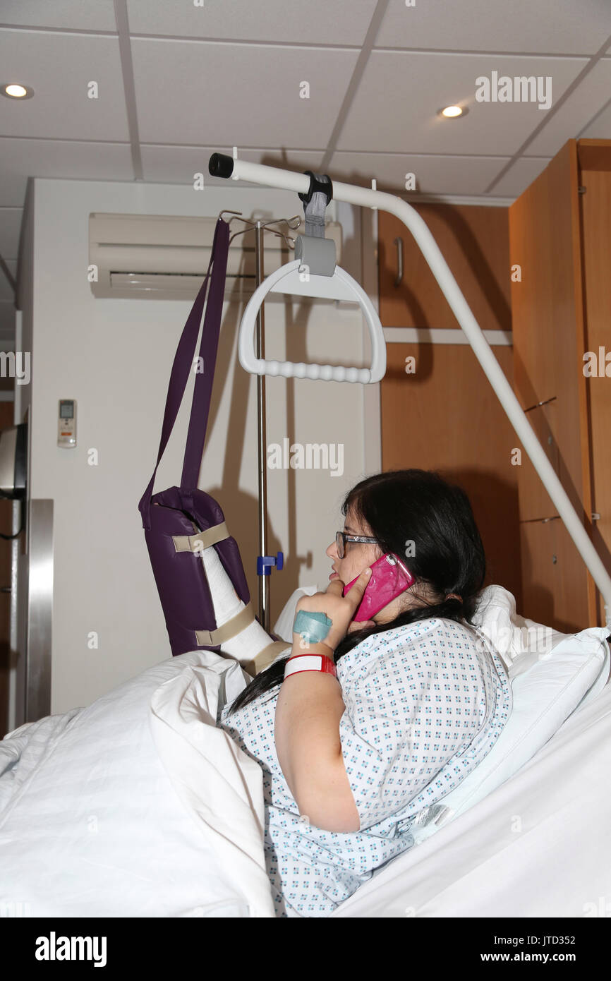 Woman in hospital using her mobile phone with other arm raised in a ...