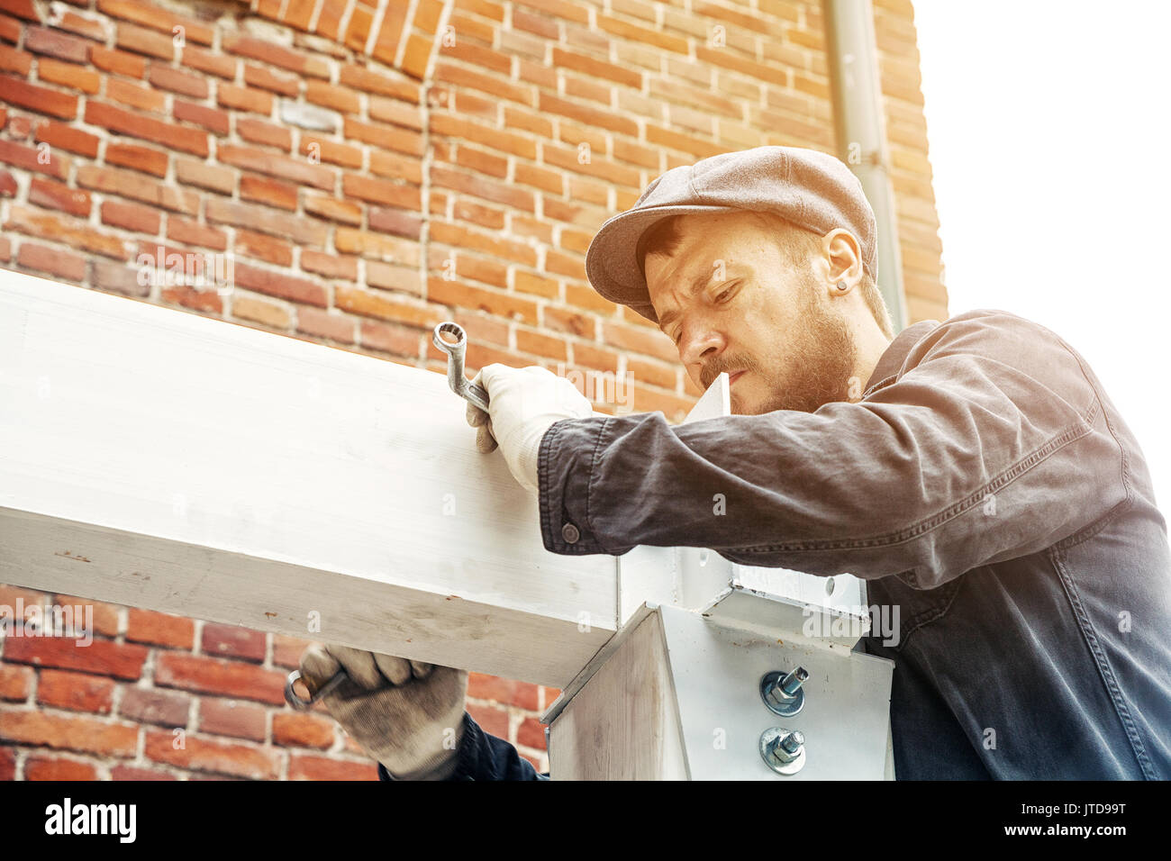 A strong man builder in dark construction overalls and a gray cap ...