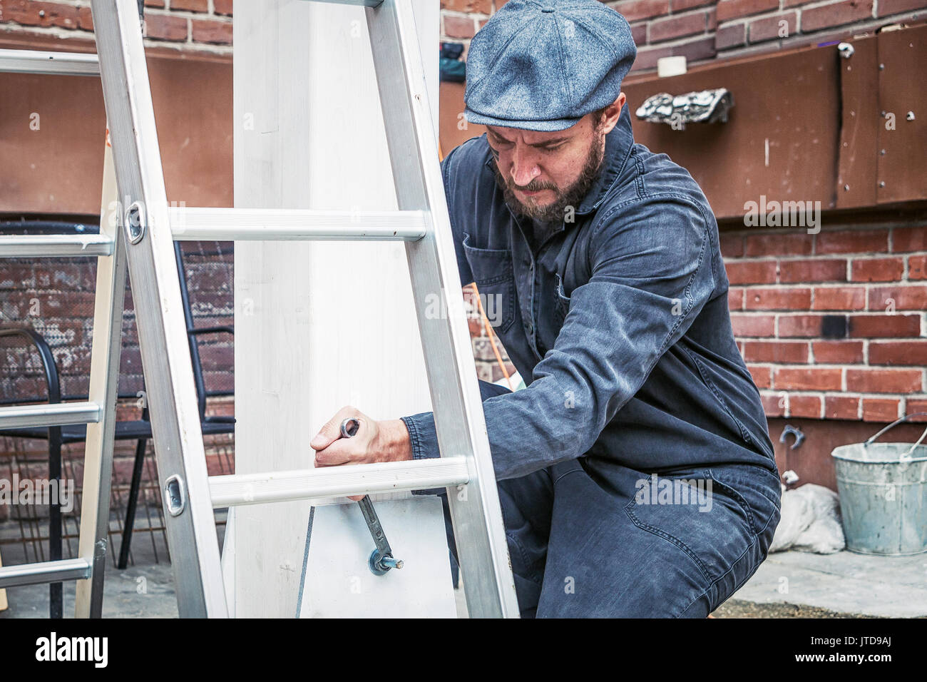 A strong construction man in dark construction overalls and a gray cap ...
