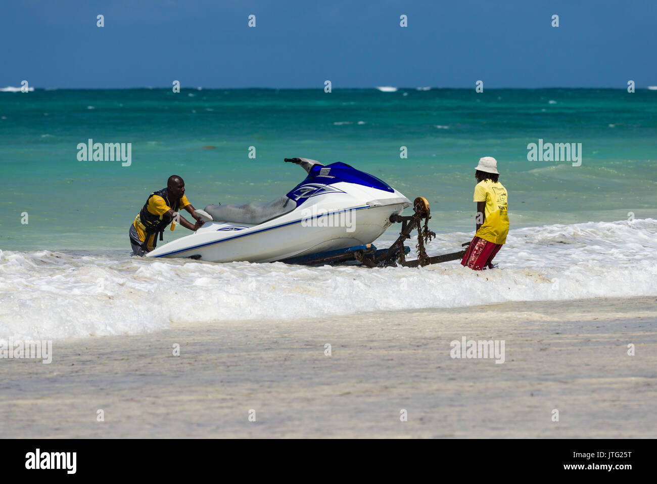 Two men pushing jet ski on to trailer in surf, Diani, Kenya Stock Photo ...