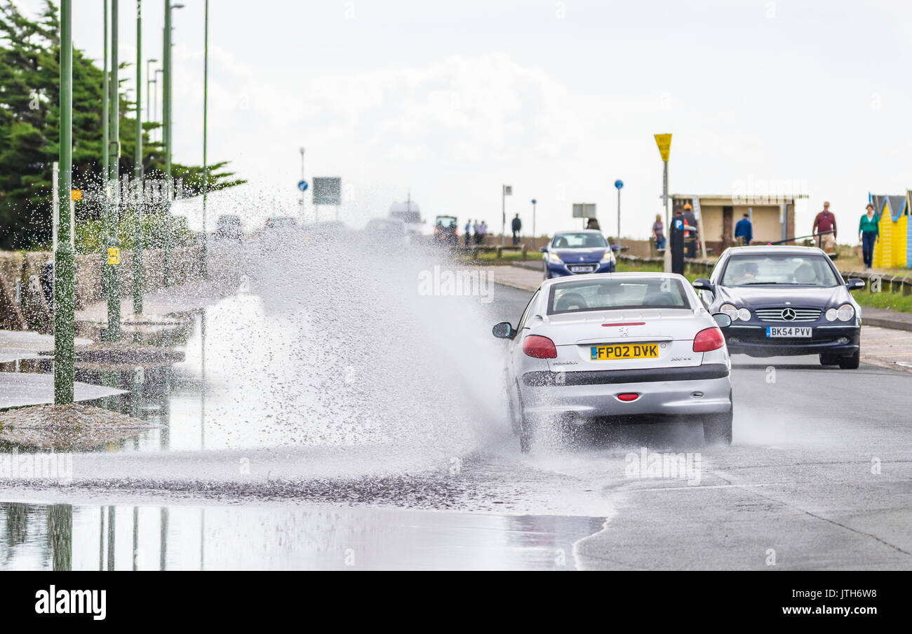 Car driving through and splashing in a large puddle where the road is ...