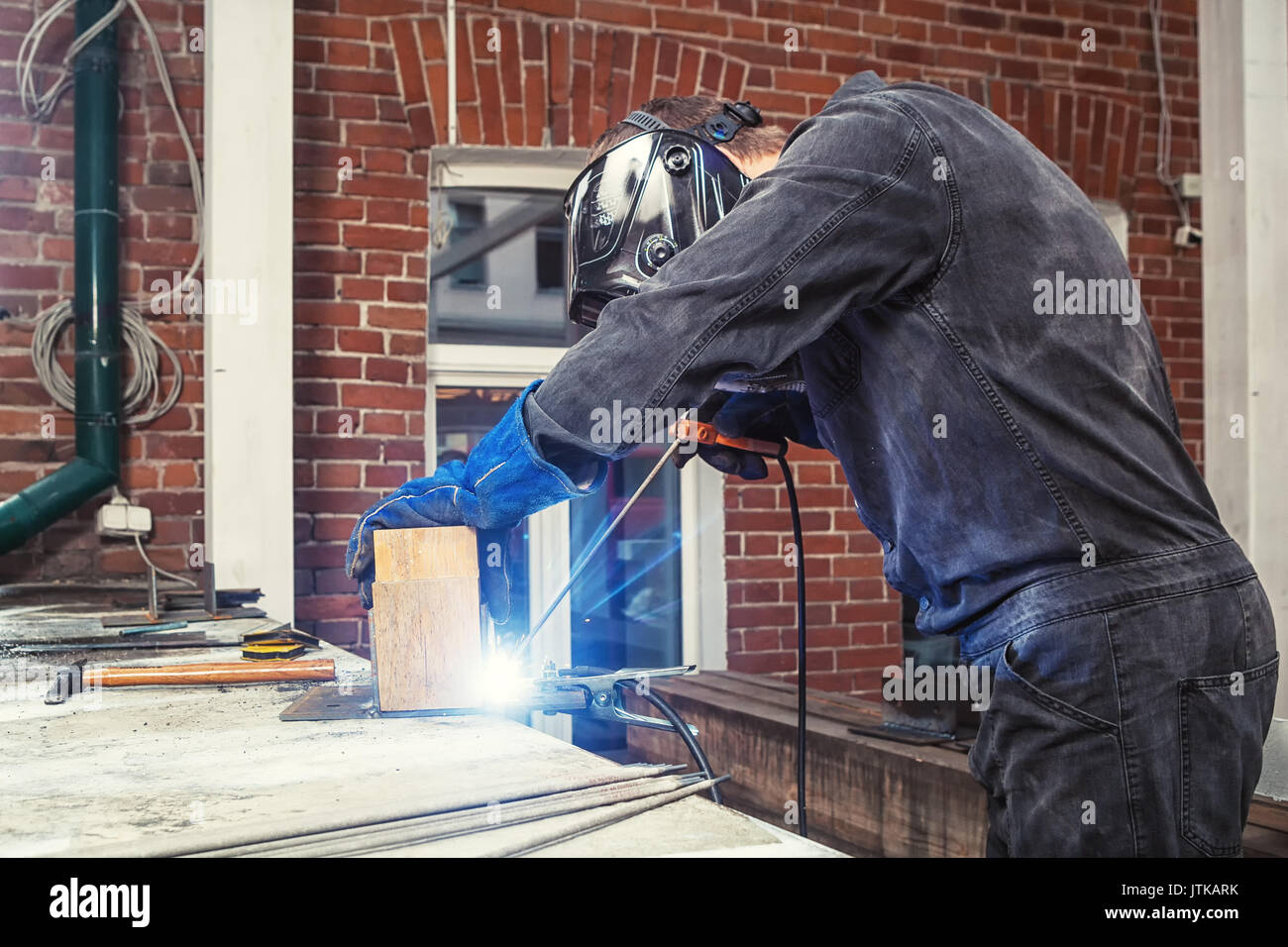A strong male welder in a construction black overall and welding swab ...