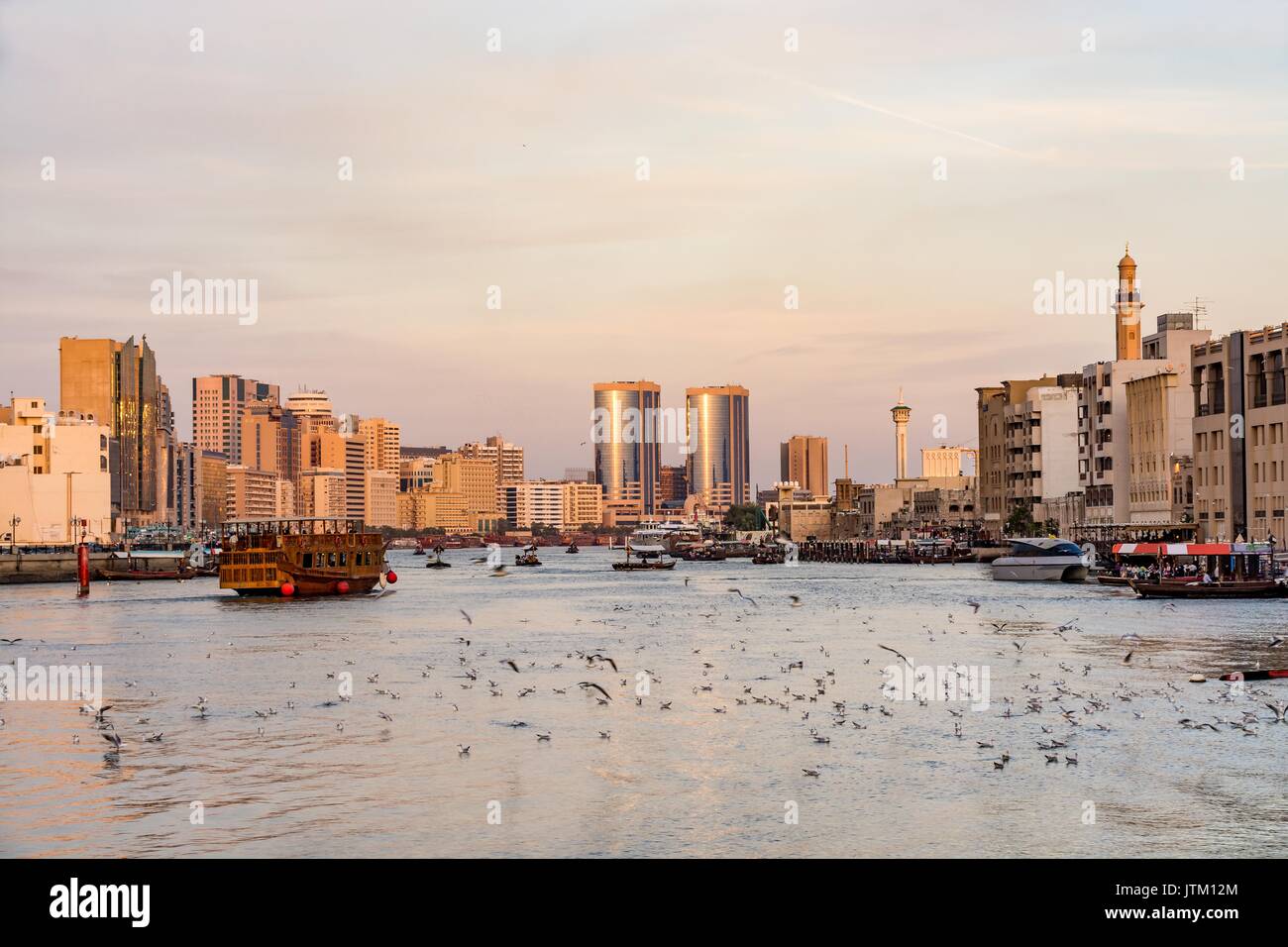 View of Dubai creek with lots of seagulls and abra boats at sunset ...