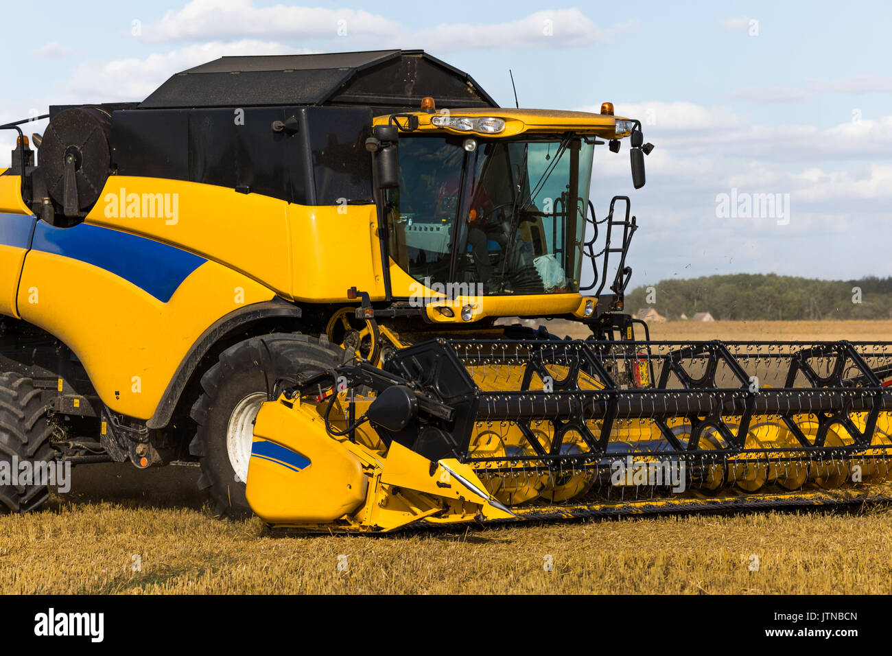 Yellow combine harvester on a wheat field with blue sky Stock Photo - Alamy
