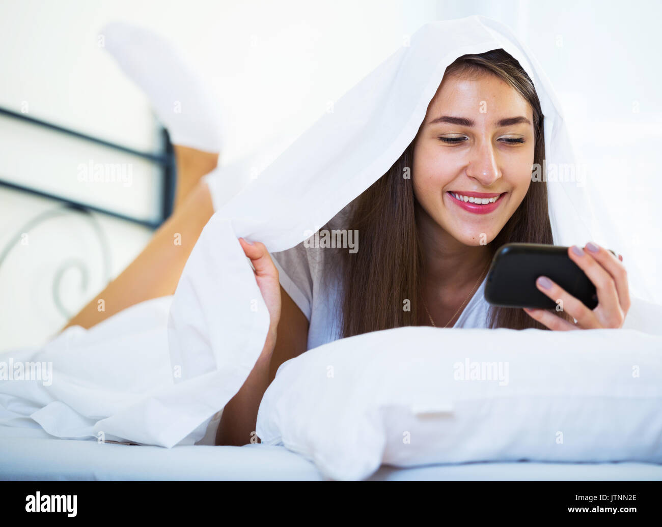 Teen female hiding under blanket with mobile phone and smiling Stock ...